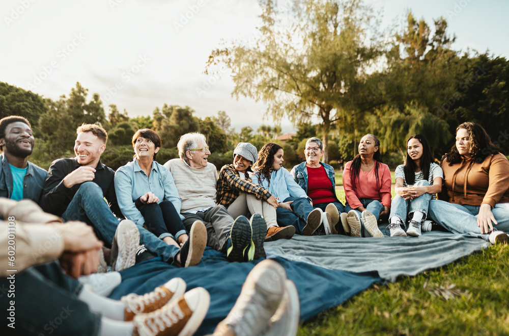 Happy multi generational people having fun sitting on grass in a public ...