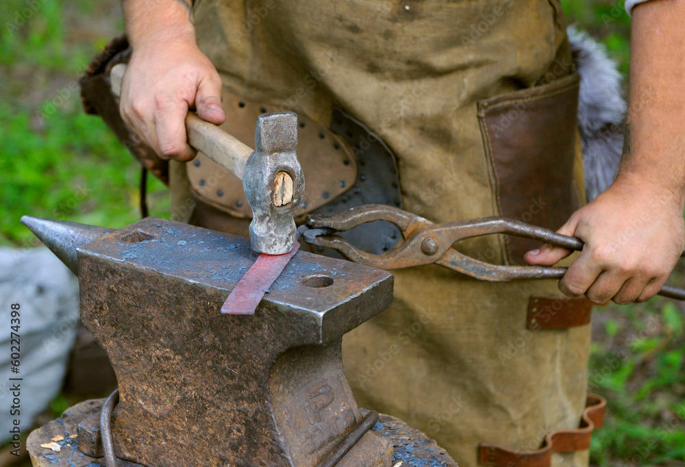 Blacksmiths hands holding forceps and hammer forging a metal billet ...