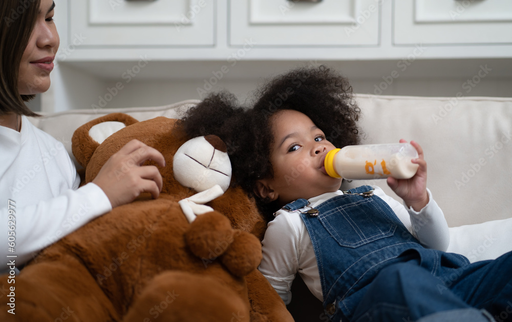 Stock-Foto „Cute biracial little girl sucking milk from bottle. Asian mother take care her ...
