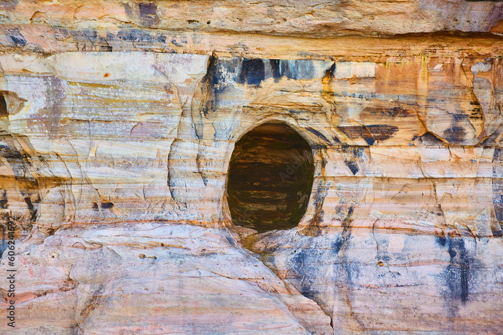 Cave opening in Pictured Rocks cliff wall of gold, rust, and mineral ...