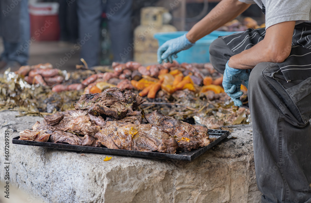 A man sets aside and puts on a tray the meat prepared underground as a ...