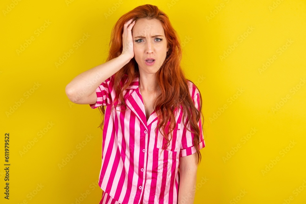 Embarrassed Young red haired woman wearing pink pyjama over yellow ...