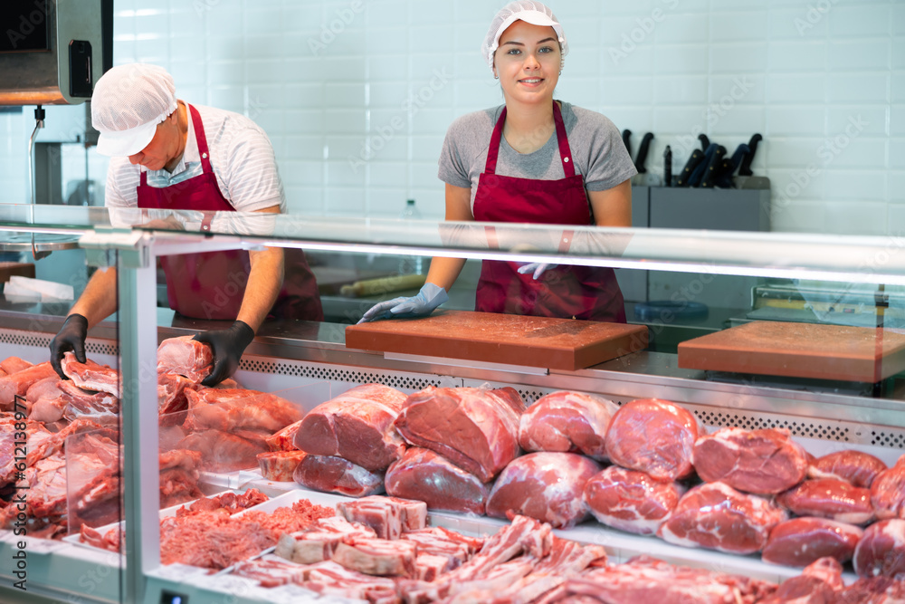 Adult man and young woman sellers in uniform display raw meat beef in ...
