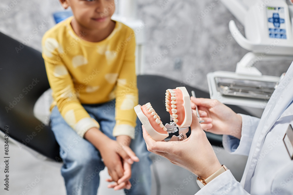 Closeup of female dentist holding tooth model and talking to child in ...