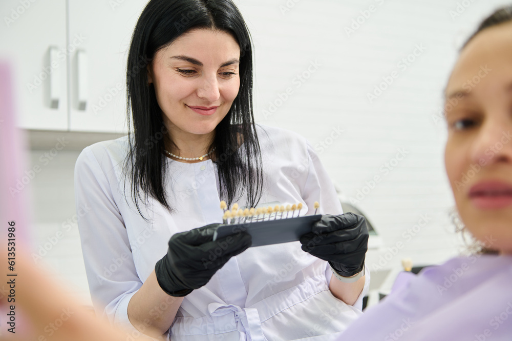 Smiling beautiful woman dentist orthodontist holding teeth color and shade chart guide according ...