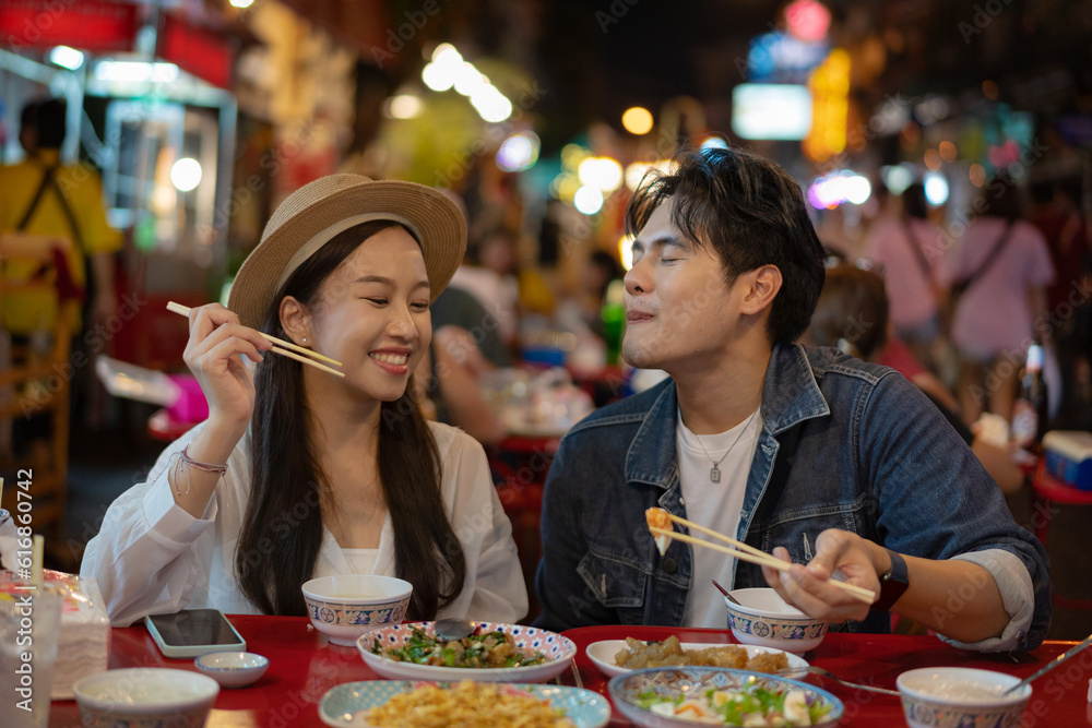 Young Asian couple traveler tourists eating Thai street food together in China town night market ...