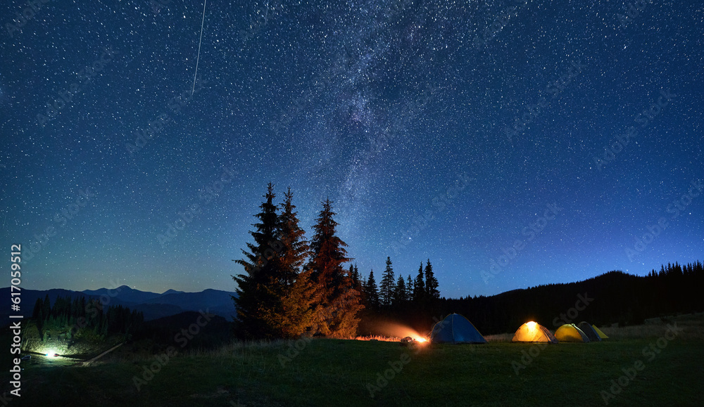 Night camping in mountains under starry sky. Tourist tents in campsite near burning campfire ...