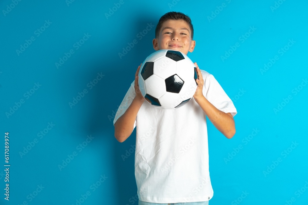 Little hispanic boy wearing white T-shirt holding a football ball ...