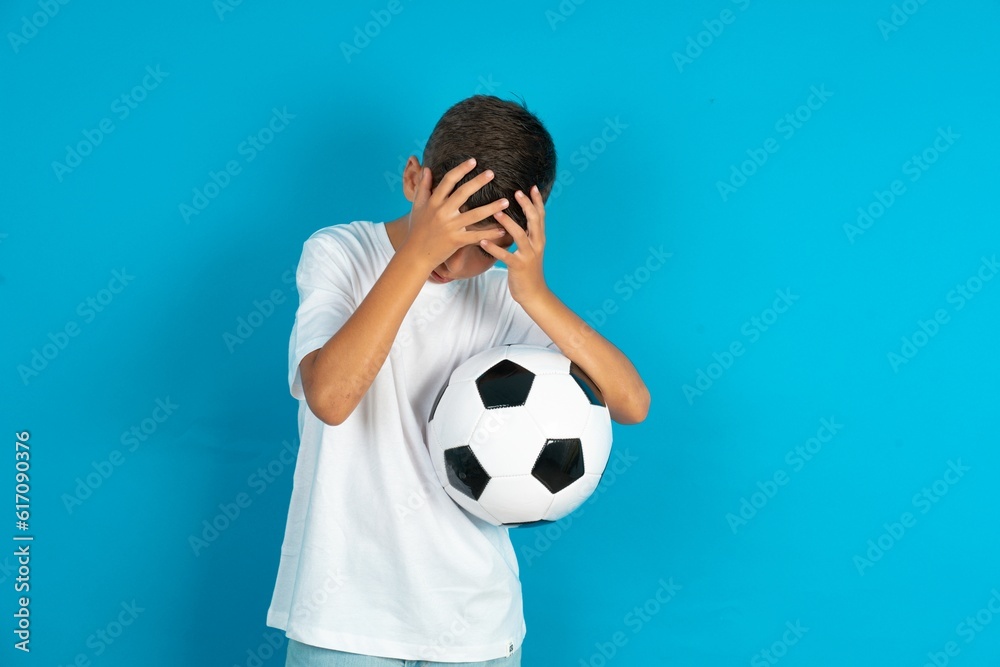 Little hispanic boy wearing white T-shirt holding a football ball ...