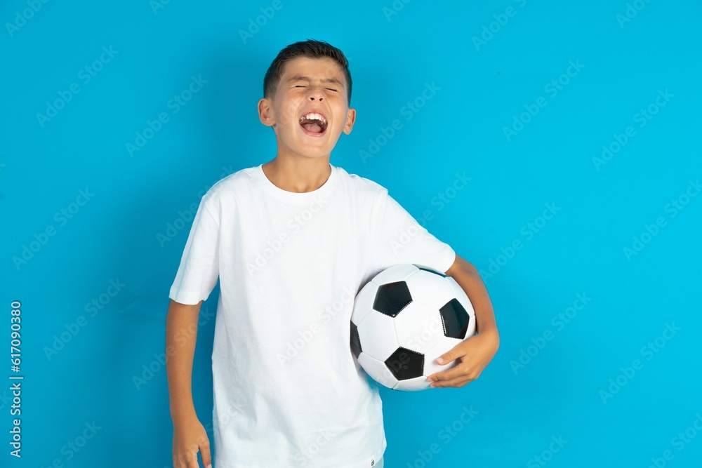 Fotografie Little hispanic boy wearing white T-shirt holding a football ...