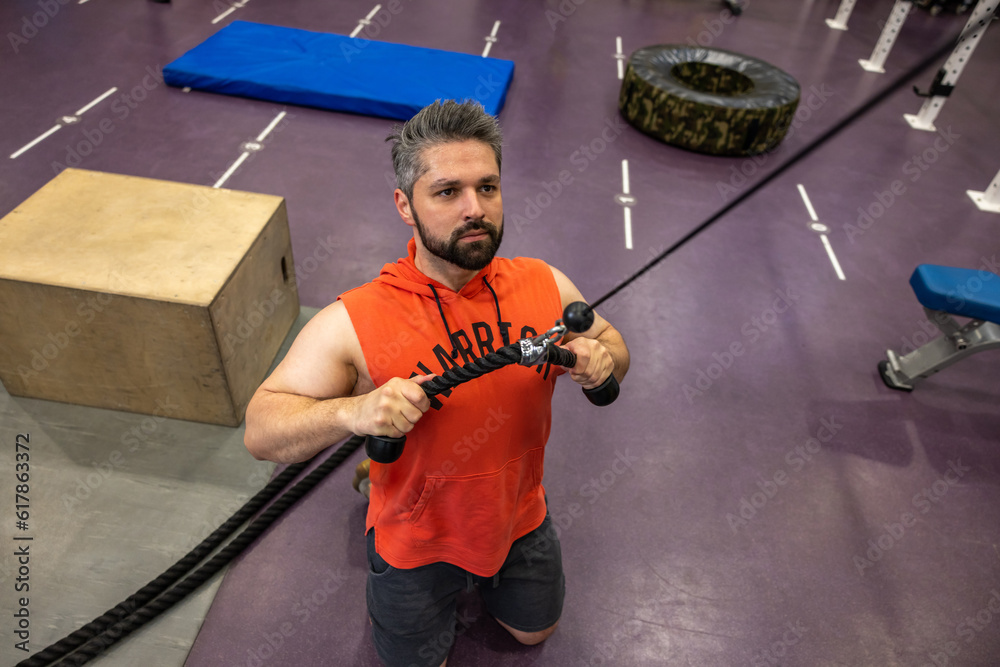 Strong sporty man training triceps and biceps at gym, doing cable rope ...