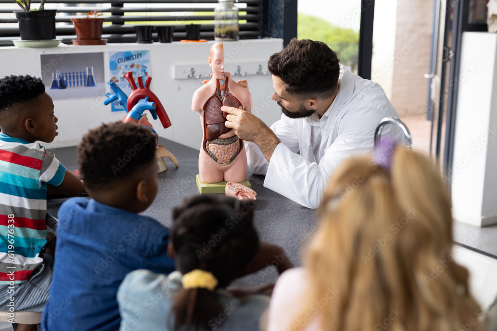 Diverse elementary school pupils and male biology teacher studying ...