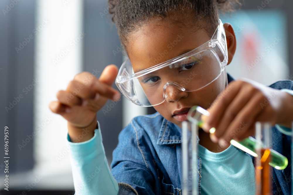 Serious biracial schoolgirl in safety glasses doing experiment in ...