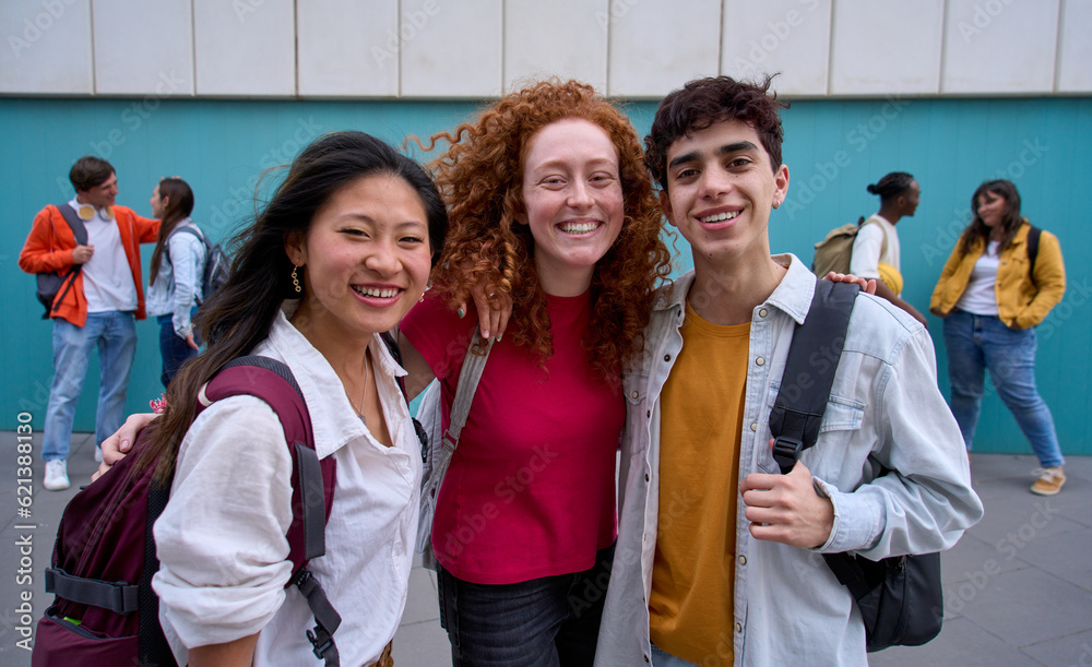 Group portrait of three smiling multiracial students hugging backpacks ...