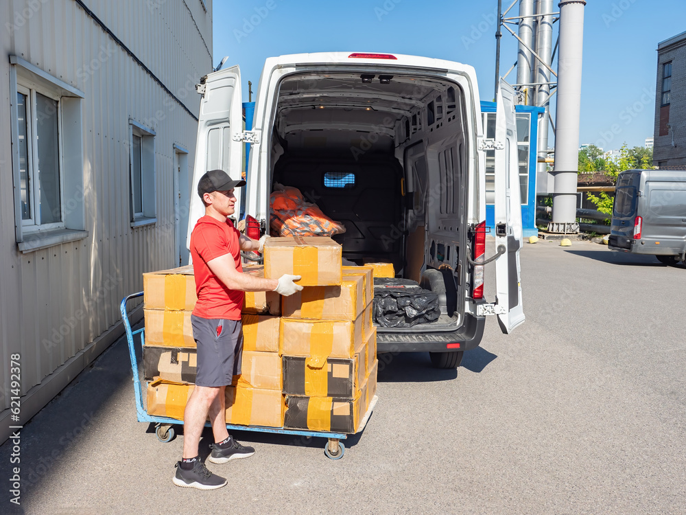 Delivery man with boxes. Loading goods into minivan. Delivery man is ...