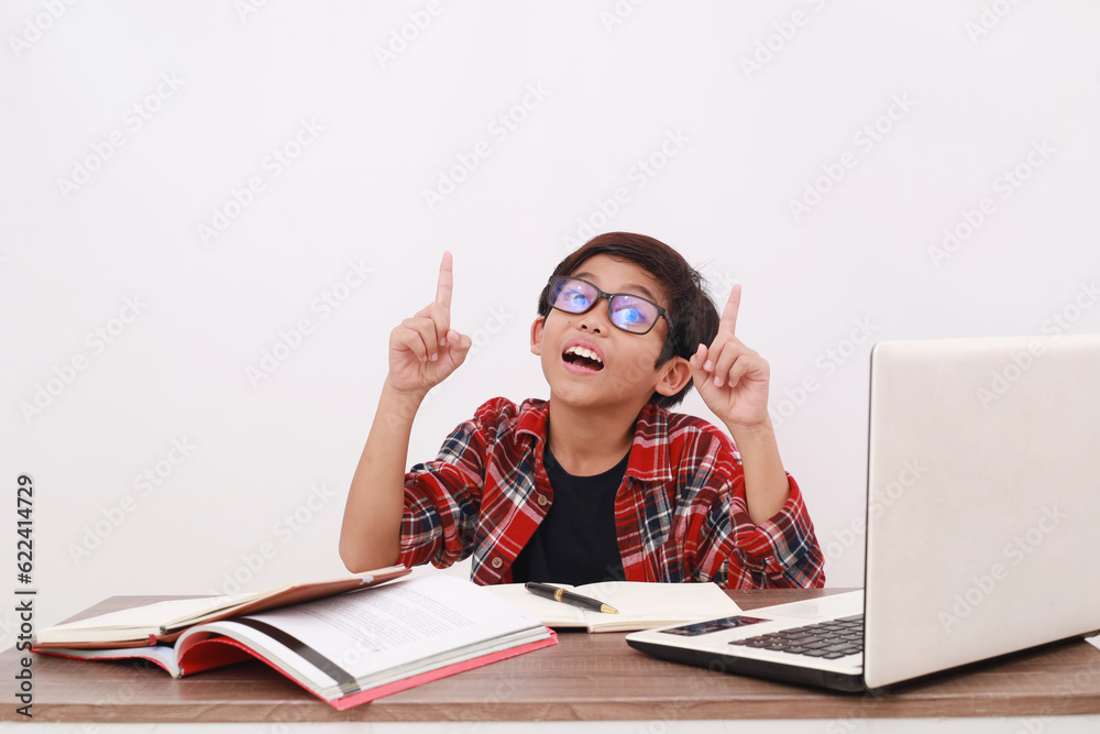 Excited Asian student pointing above while studying with books and ...