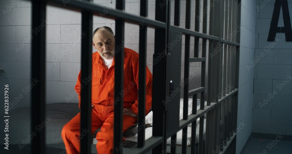 Elderly criminal in orange uniform sits on prison bed and thinks about ...