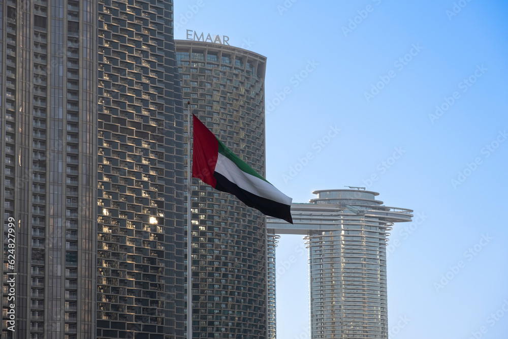 UAE flag waving on a mast against blue sky with highrise skyscraper ...