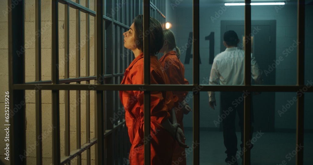 Two female prisoners, inmates in orange uniforms stand facing the metal ...