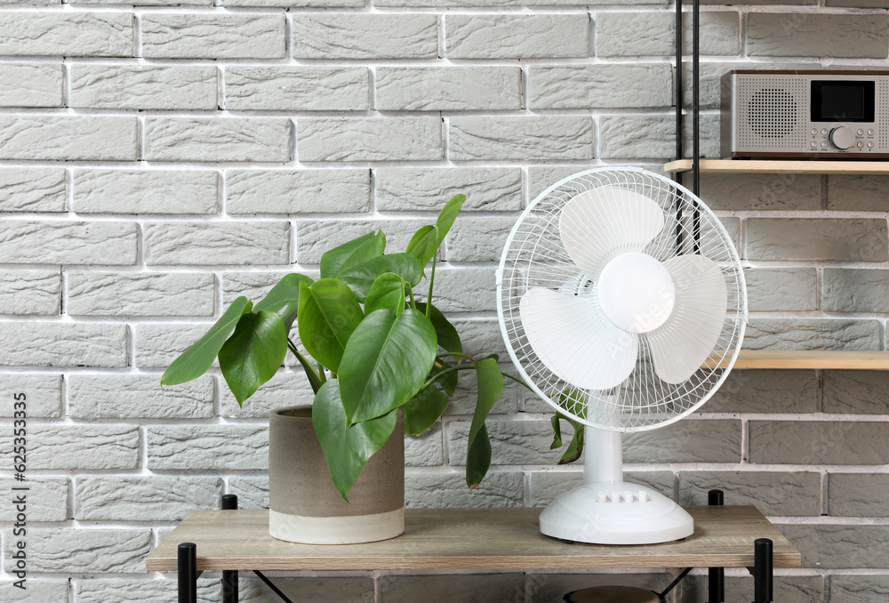 Electric fan with houseplant on shelf near grey brick wall in room ...