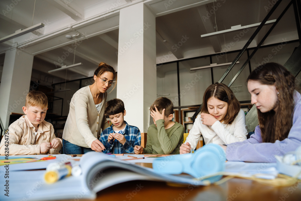 Female teacher teaching group of children drawing during art lesson in ...