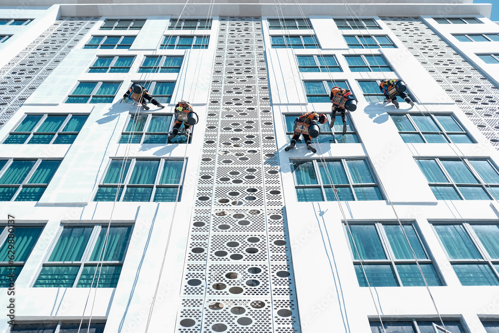 Workers climb high-rise buildings using ropes to clean window panes ...