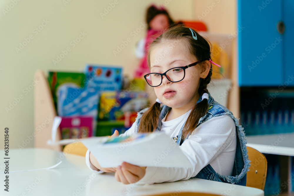 Cute little junior choolgirl with spesial needs sitting at desk at ...