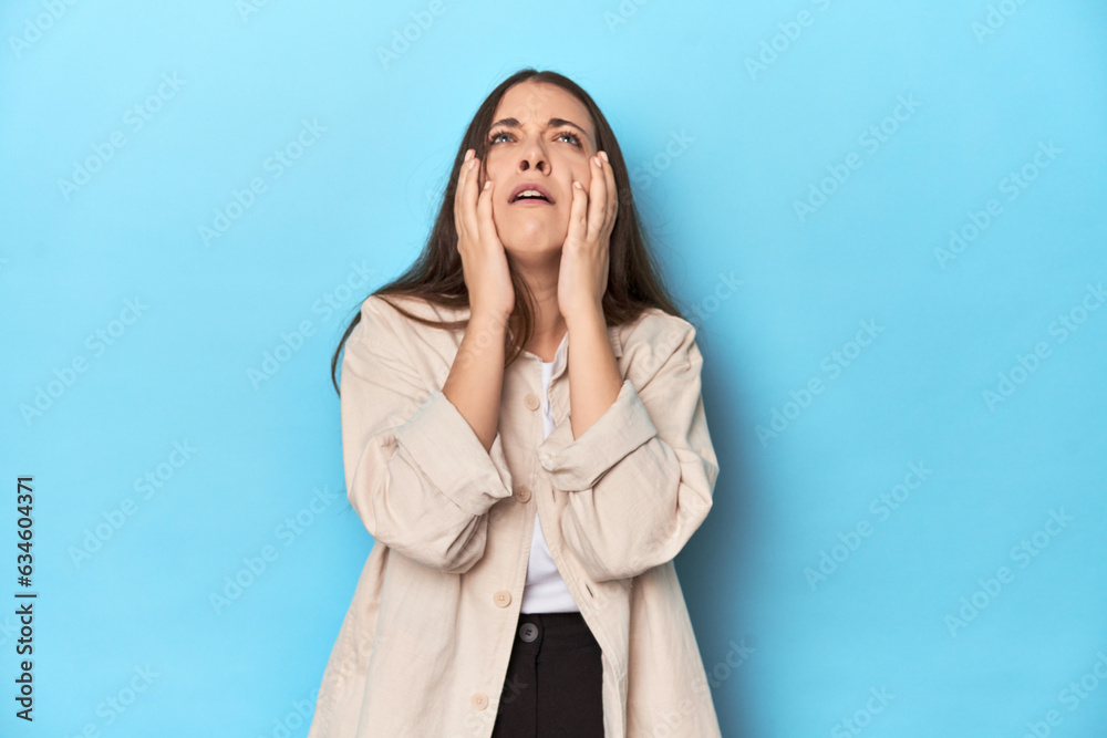 Stylish young woman in an overshirt on a blue background whining and ...