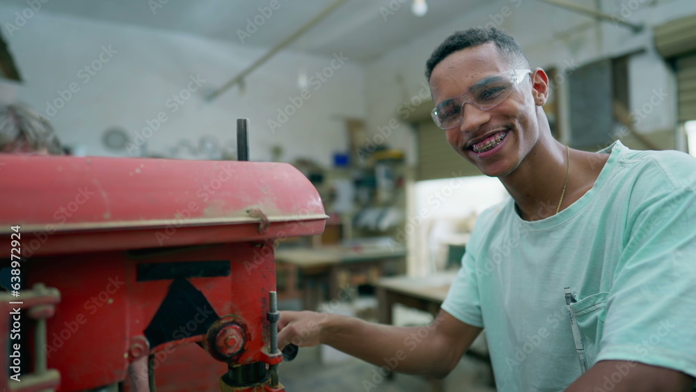 One happy young black carpentry apprentice using industrial machine ...