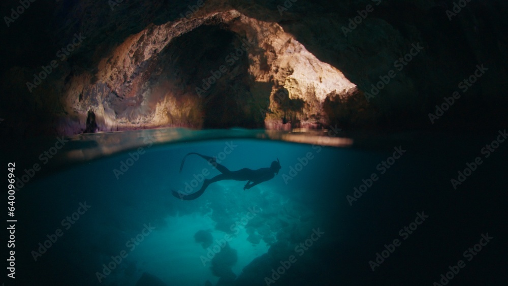 Freediver swims underwater in the cave. Male freediver explores the ...