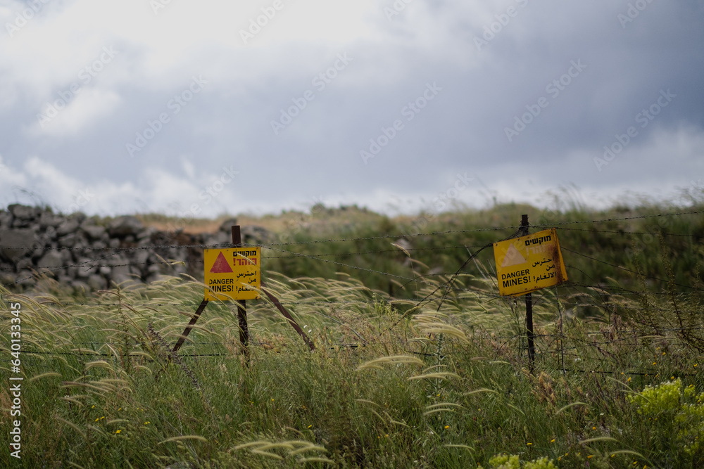 In the Golan Heights, a fence marks off an area. A bright yellow sign ...