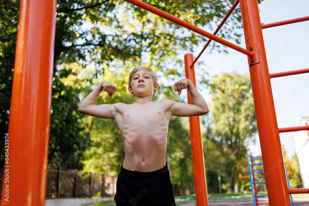 A teenager boy of an athletic build shows his muscles. Street workout ...