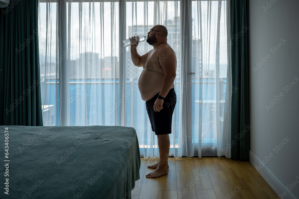 Thirsty overweight man feeling dehydration drinking water in hotel room ...