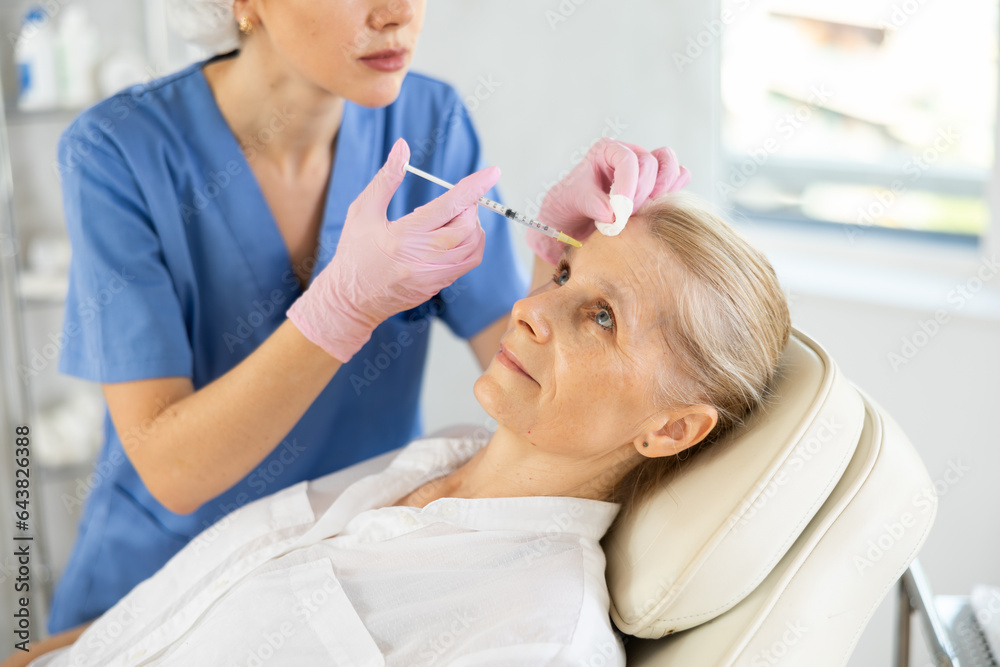Female doctor conducting face revitalization procedure for aged woman ...