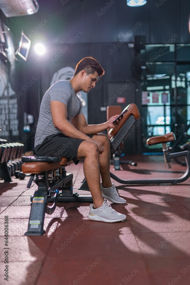 Good looking Asian man finds relaxation in the gym, using and checking ...