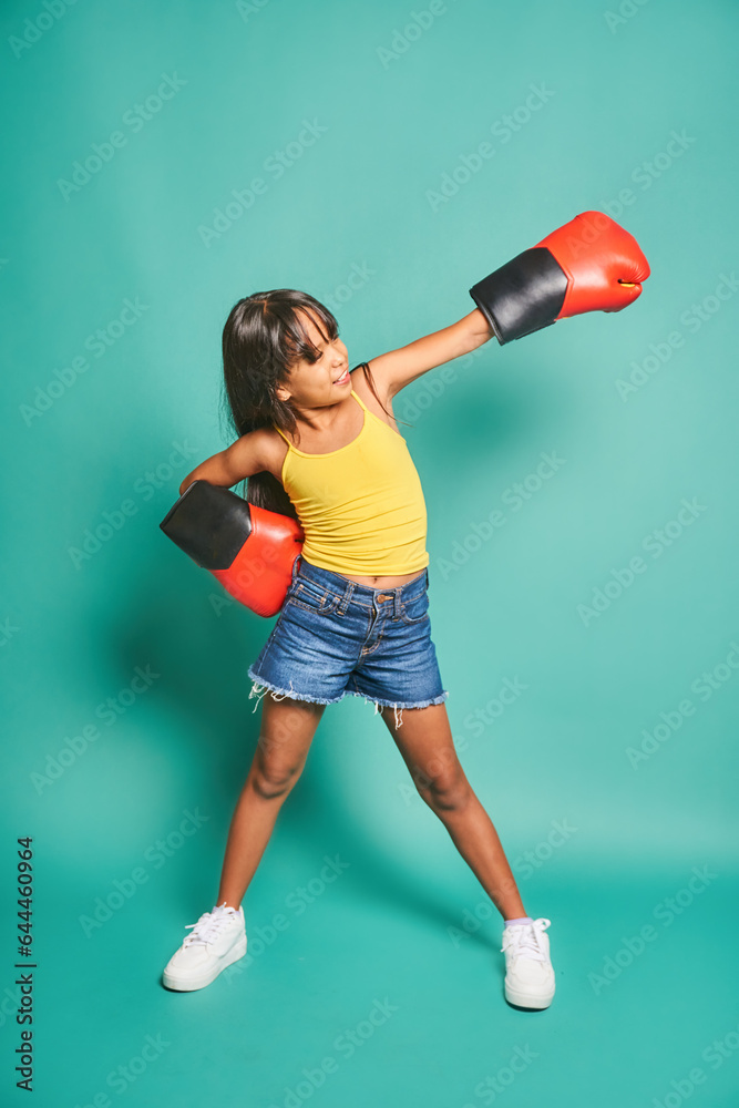 Cheerful ethnic kid girl in boxing gloves throwing punches against ...