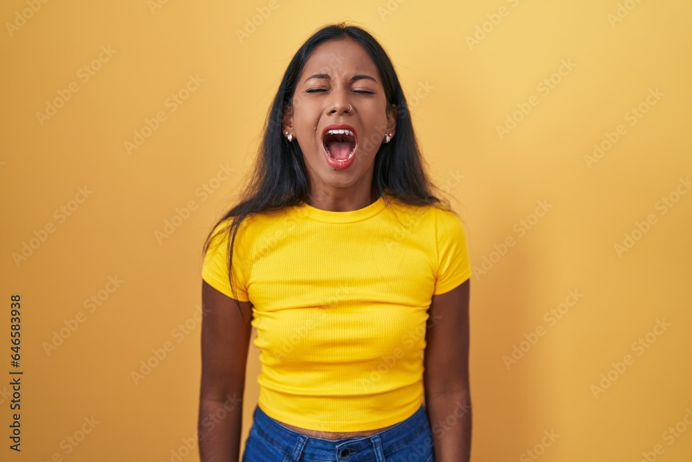 Young indian woman standing over yellow background angry and mad ...