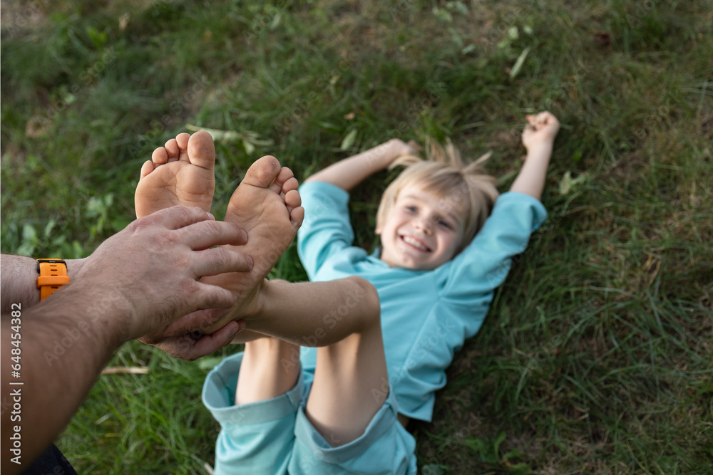 man's hands tickle a child's bare feet lying on the grass. Fun family ...