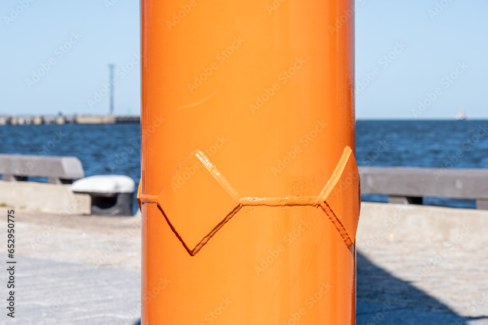 Fundament of sea buoy. A huge metal bright orange tube on the seashore ...