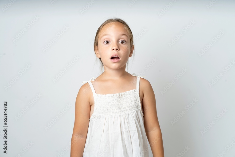 Shocked beautiful kid girl wearing white dress stares bugged eyes keeps ...