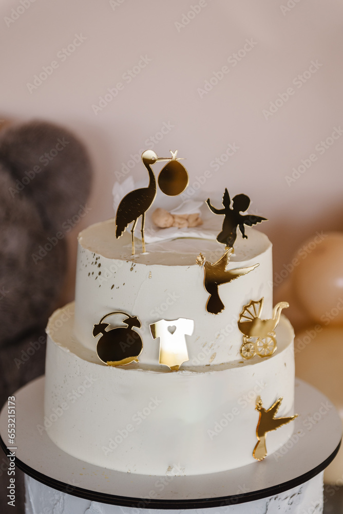 Cake with a figure angel, stork carrying a baby, and golden decor. Celebration baptism concept ...