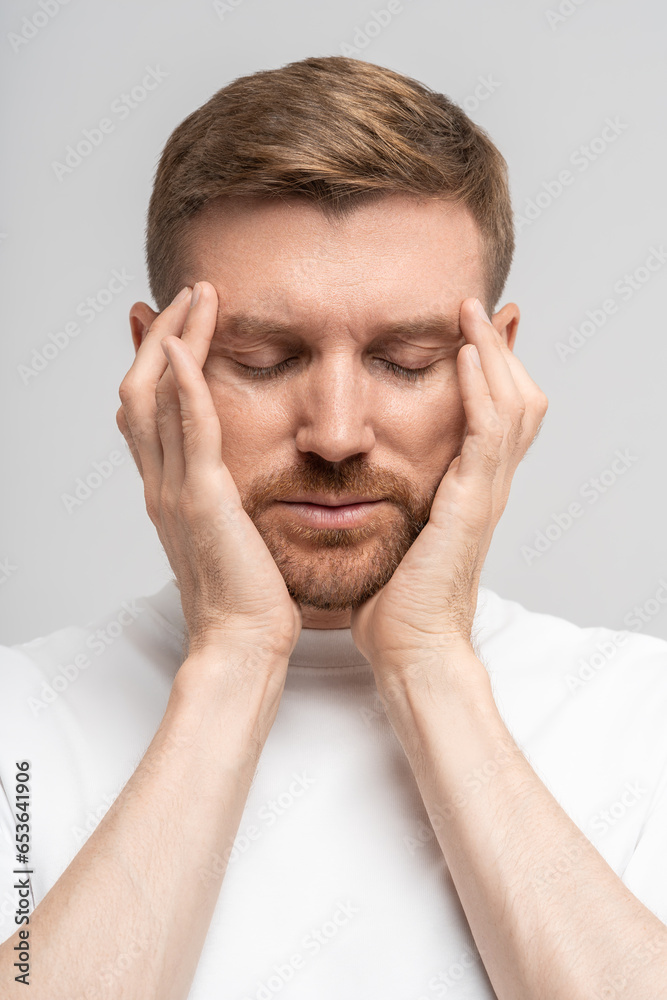 Irritated exhausted man with eyes closed presses fingers to temples ...