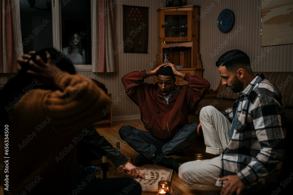 Shocked friends looking at woman touching ouija board while ghost at ...