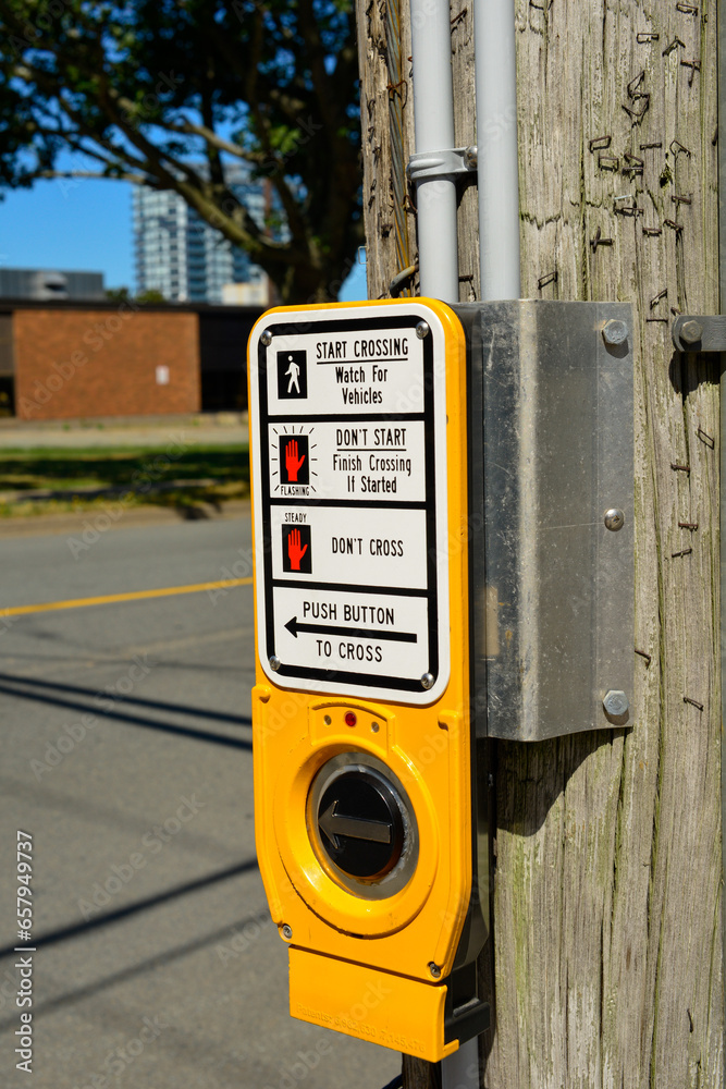 A yellow crosswalk button on a wooden utility pole at a road ...