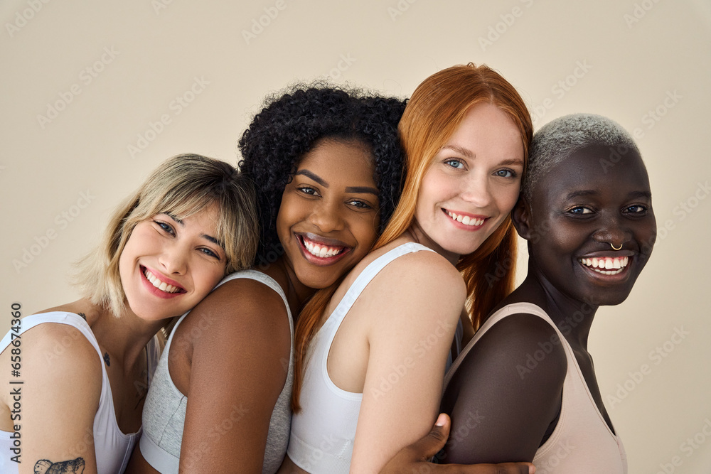 Happy multicultural girls in underwear hugging on beige background ...