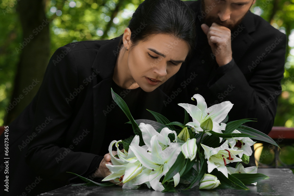 Sad couple mourning near granite tombstone with white lilies at ...