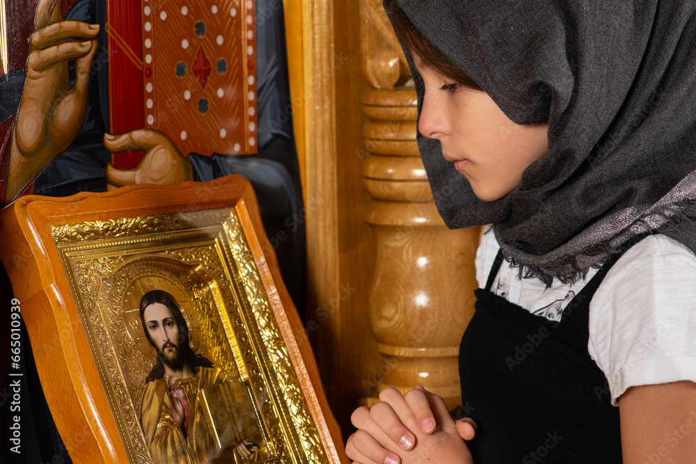 Young girl praying in front of an icon of Jesus on a church pulpit ...
