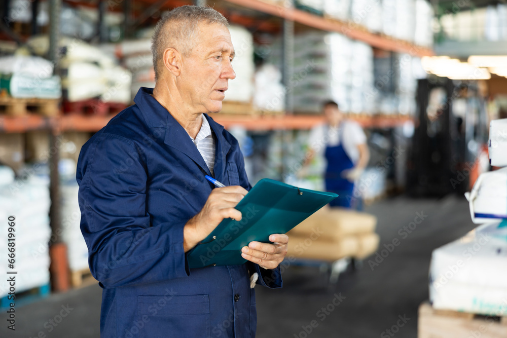 In warehouse rack area of store, mature man checks availability and ...