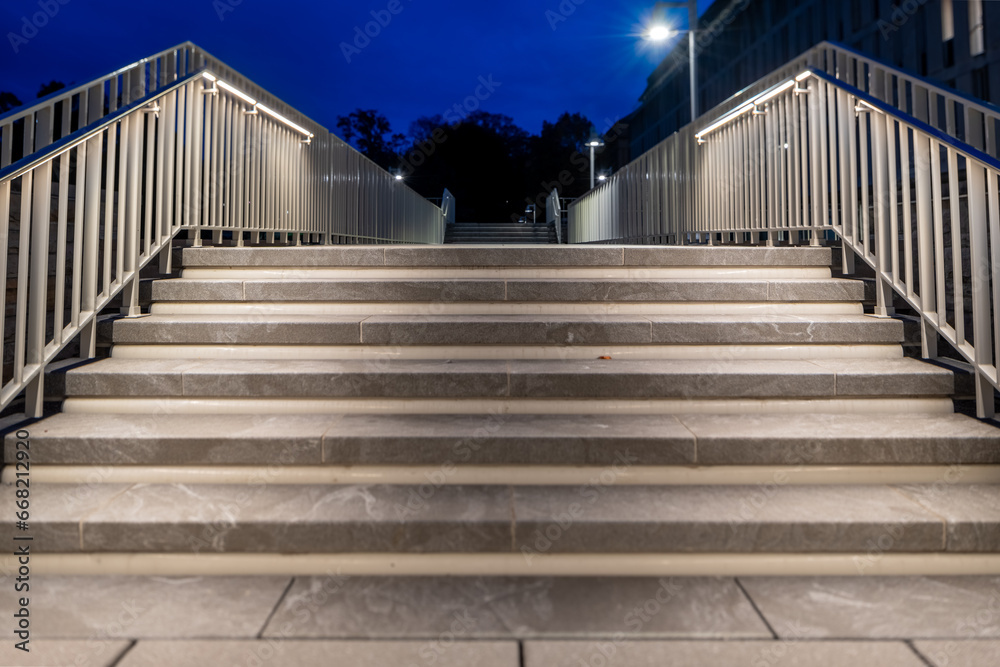 Outdoor, exterior gray stone staircase at night with chrome railings ...