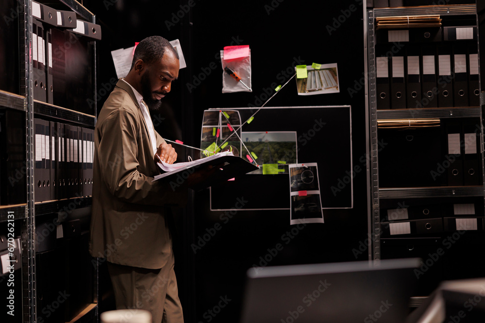 African american cop reading case file and studying detective board ...